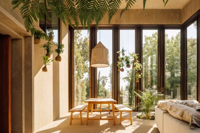 Vardagsrum i trädgårdspaviljongen av Bak Gordon Arquitectos med bankettbord och bänkar och hängande växter