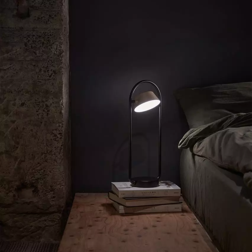 مصباح طاولة OLO في غرفة نوم مطلية باللون الداكن موضوعة فوق كومة من الكتب بجوار السرير