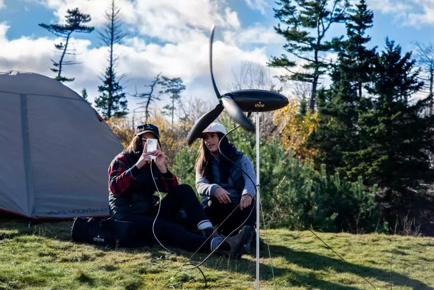 Éolienne installée devant deux personnes assises devant leur tente en pleine nature