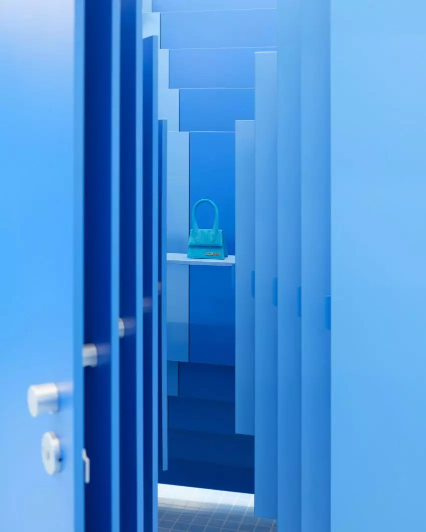 Uma bolsa Jacquemus é retratada atrás das portas azuis do cubículo